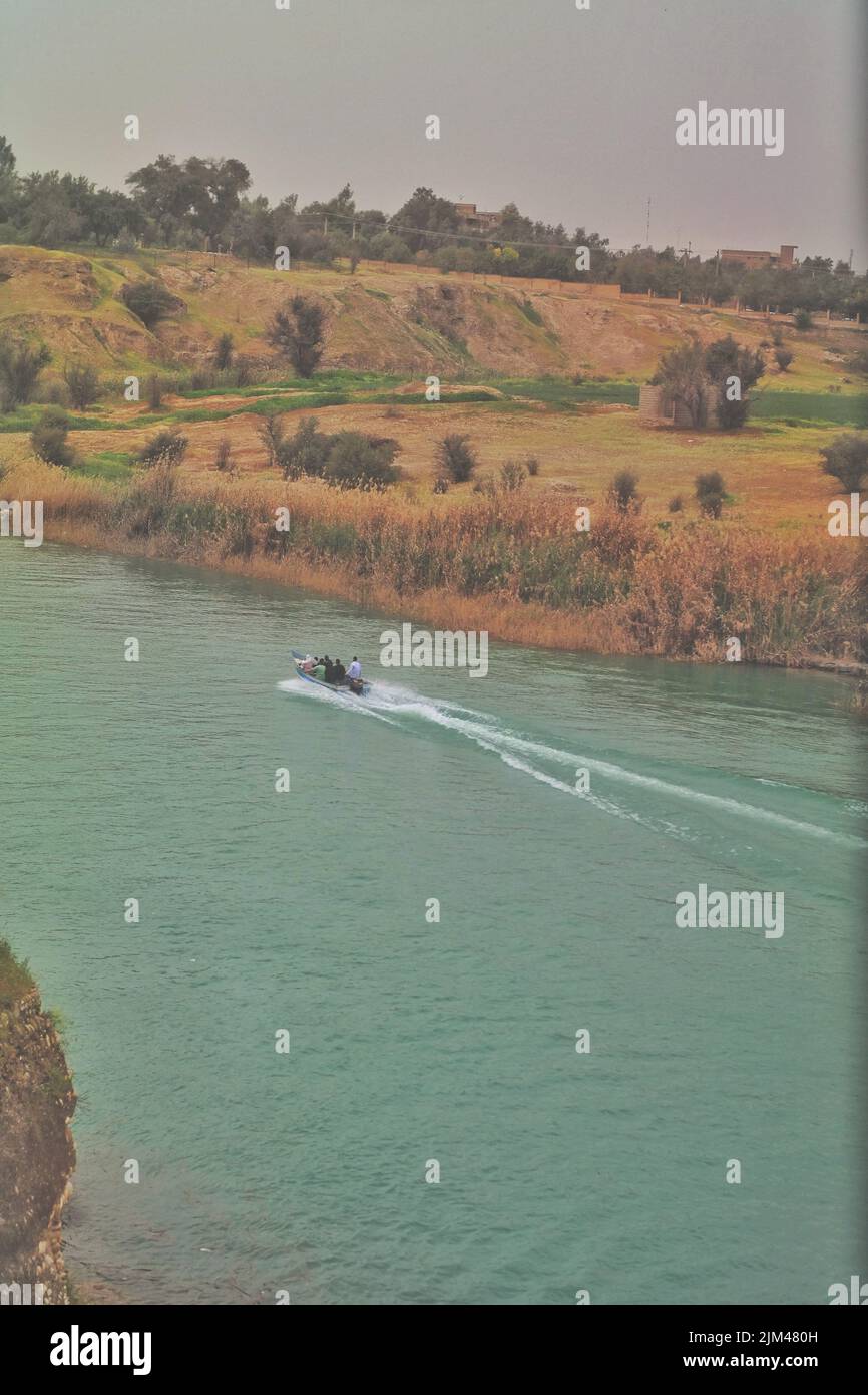 A vertical distant view of a boat with people sailing across a river ...