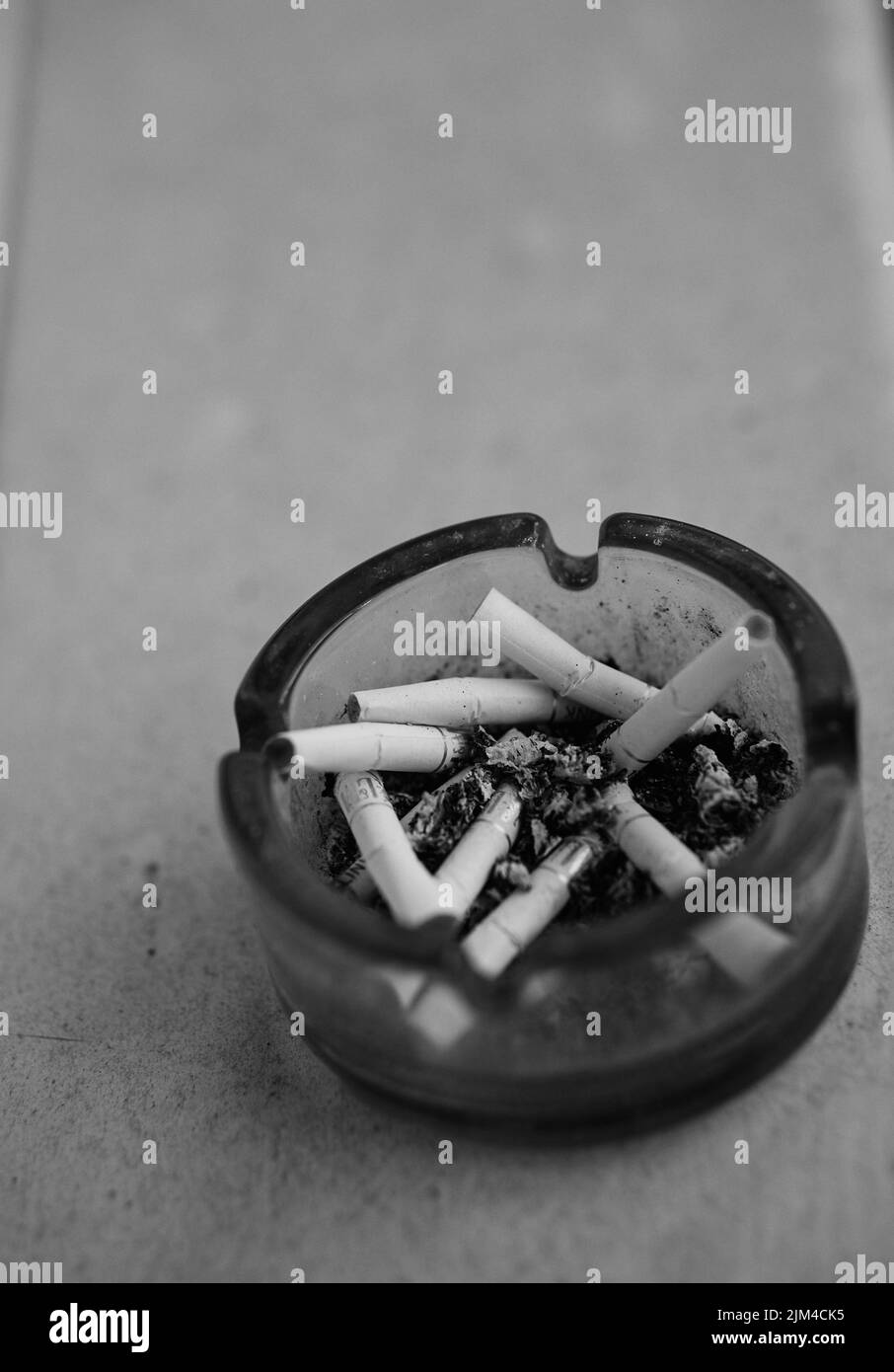 A vertical closeup of cigarette buds in a full ashtray in grayscale ...