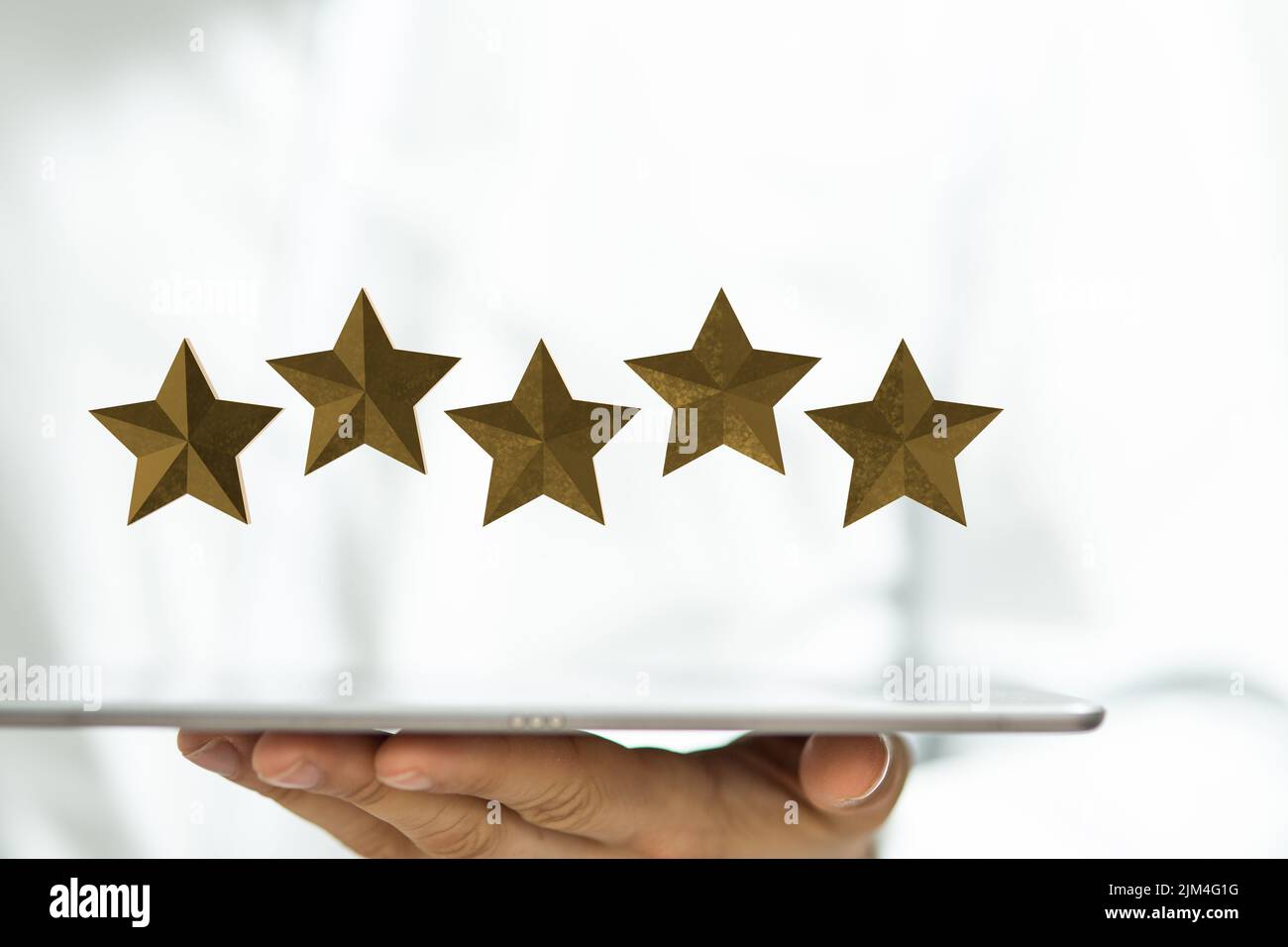 A closeup of a hand holding illustrated 3D five stars above a tablet ...