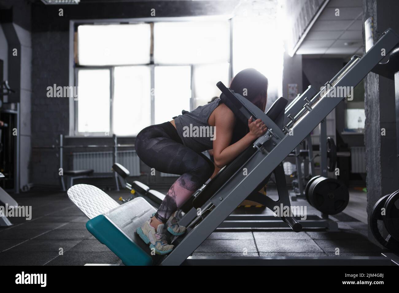 Profile shot of a strong athletic woman doing squats in hack squat gym ...