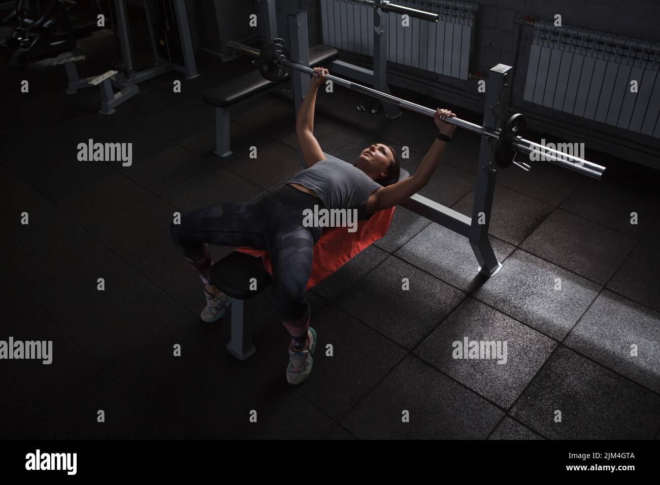 Top view shot of a fitness woman doing barbell bench press in dramatic ...