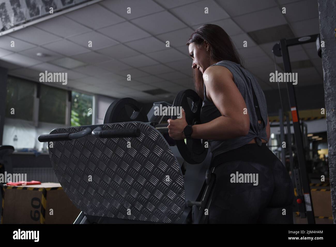 Low angle shot of a female bodybuilder putting weights on leg press ...