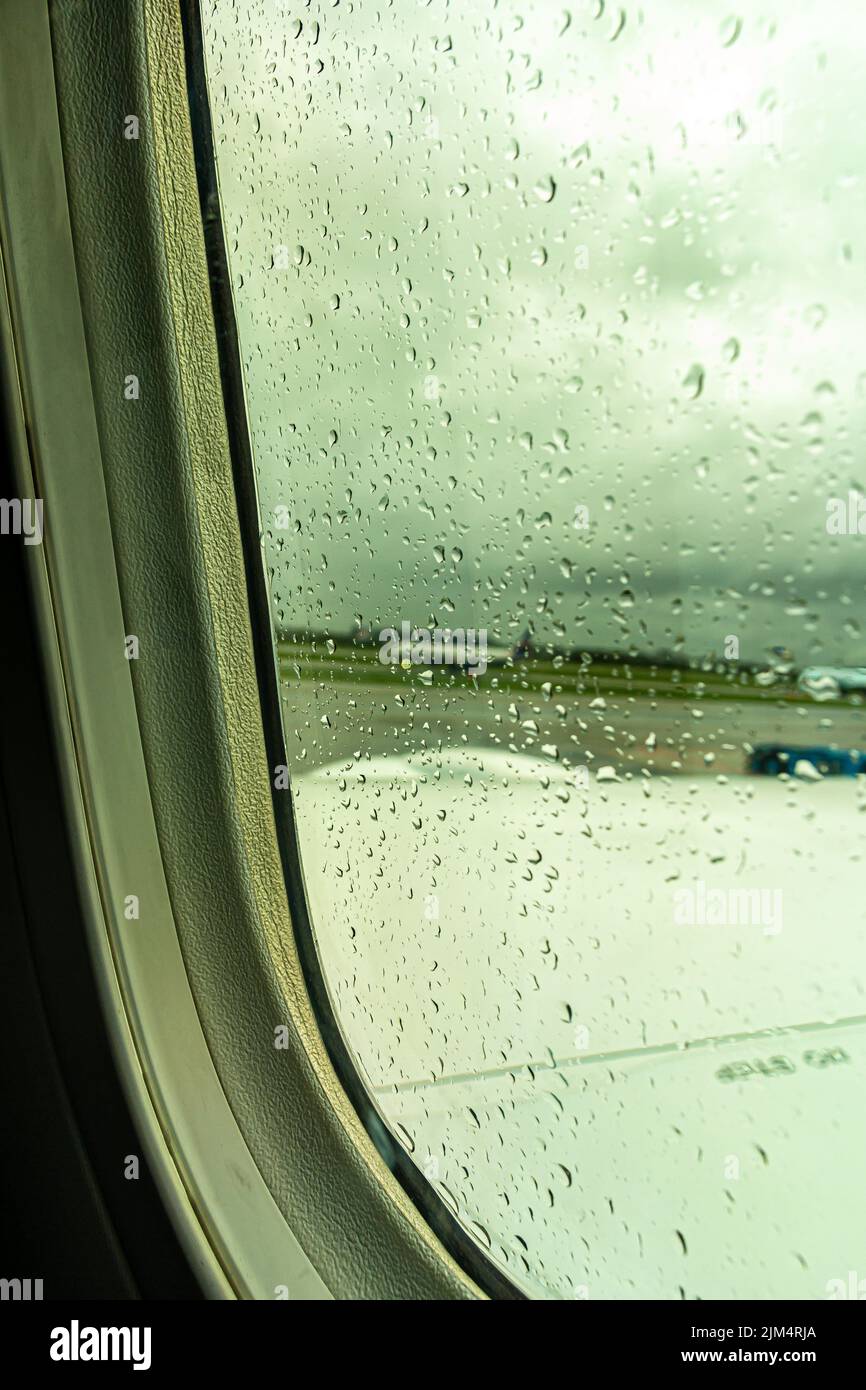 View of airplane wing through passenger window with rain drops at rainy ...