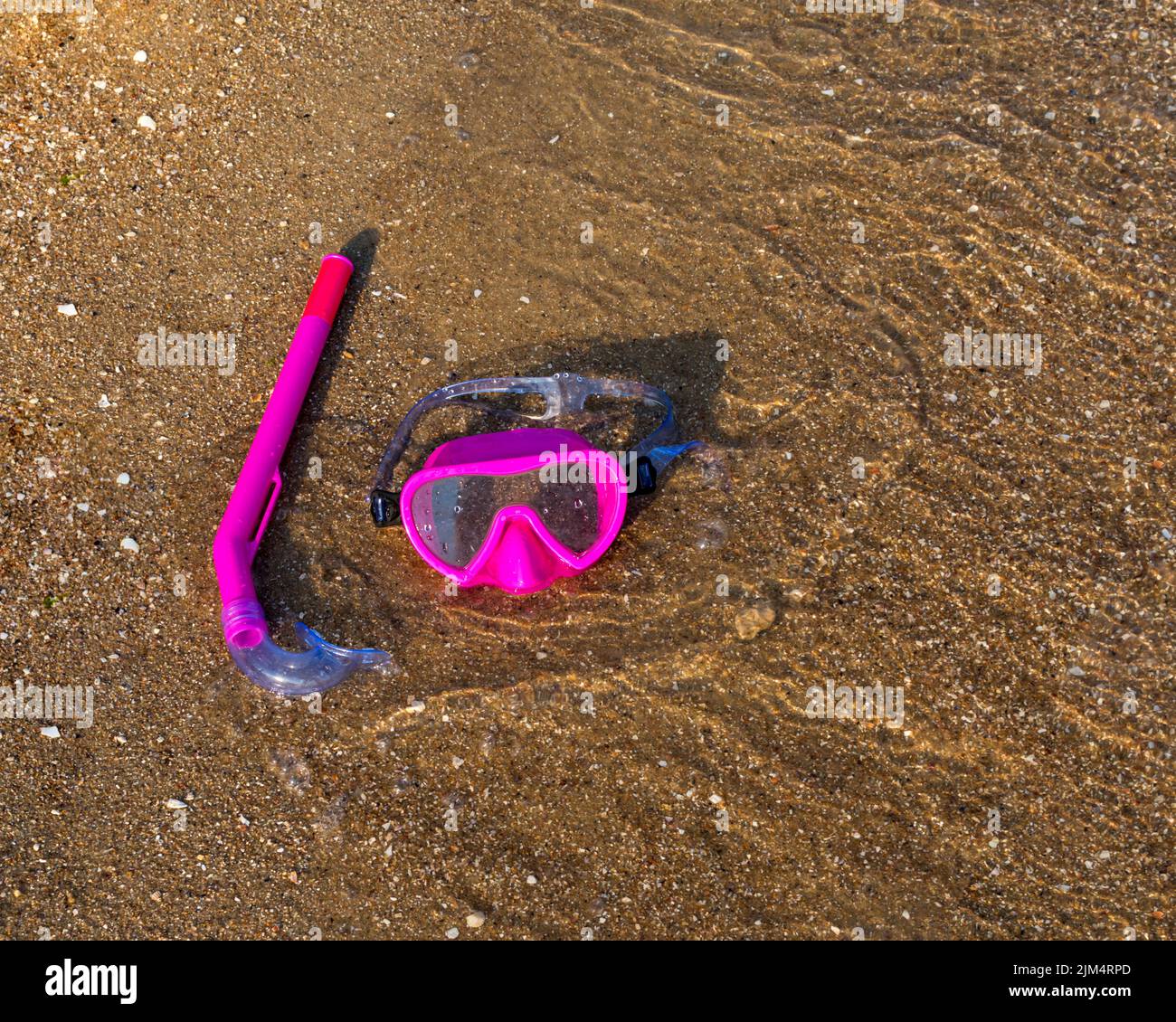 Pink swimming mask and diving snorkel lie on the sand near the water ...