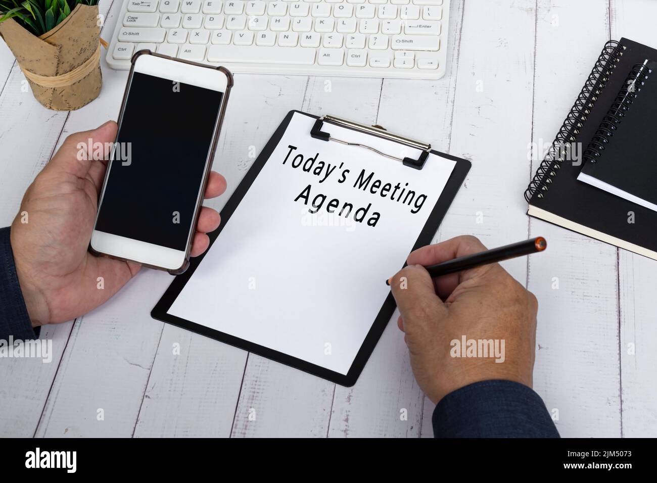 Hand with pencil writing Today's Meeting Agenda on the black clipboard ...