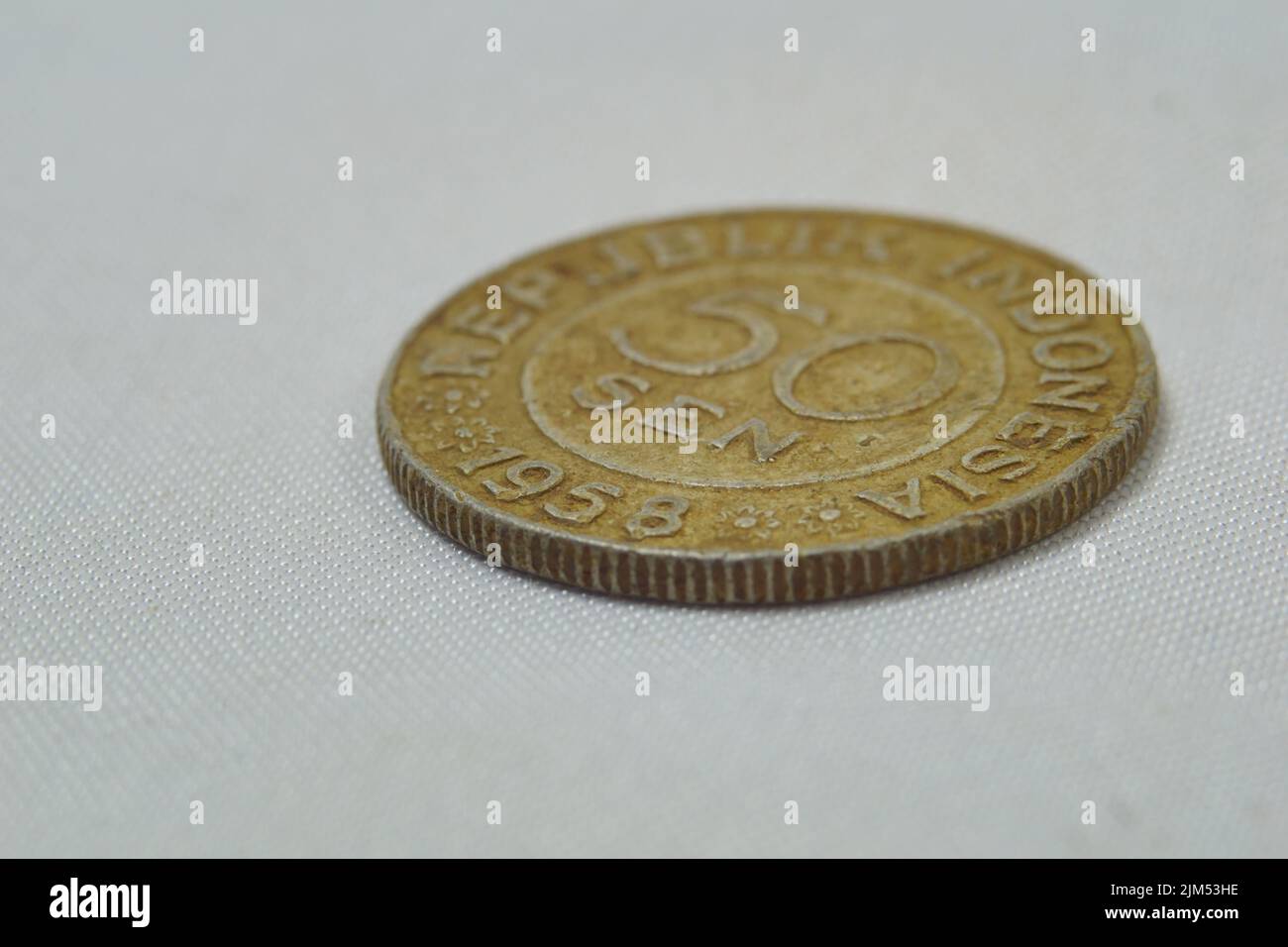 A closeup of a 50 sen Indonesian coin from 1958 on a white background ...