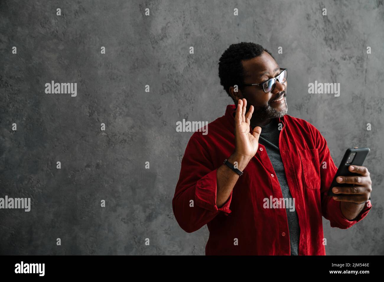 Black man waving hand and using cellphone while standing by concrete ...
