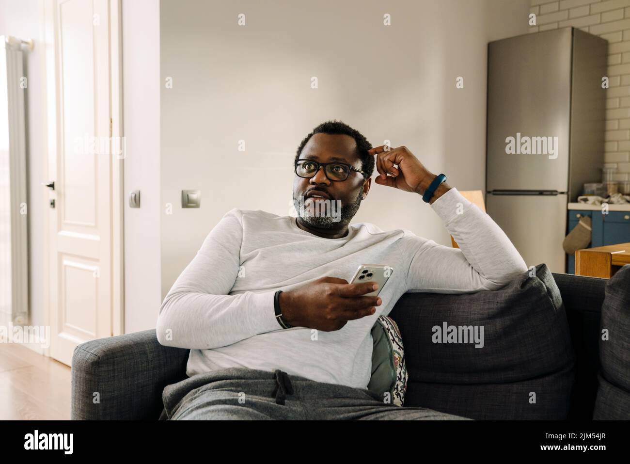 Black man using mobile phone while watching tv on sofa at home Stock ...