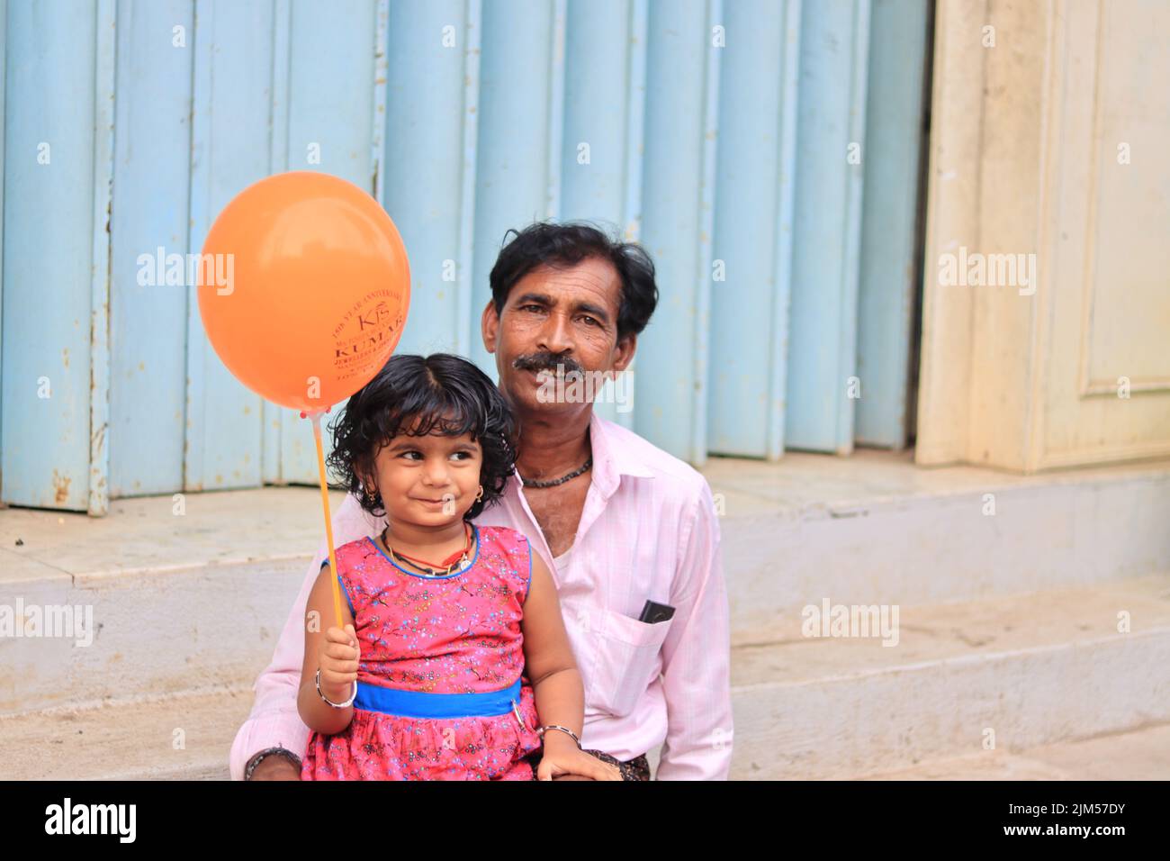 A grandfather carrying his granddaughter holding a balloon in his arms ...