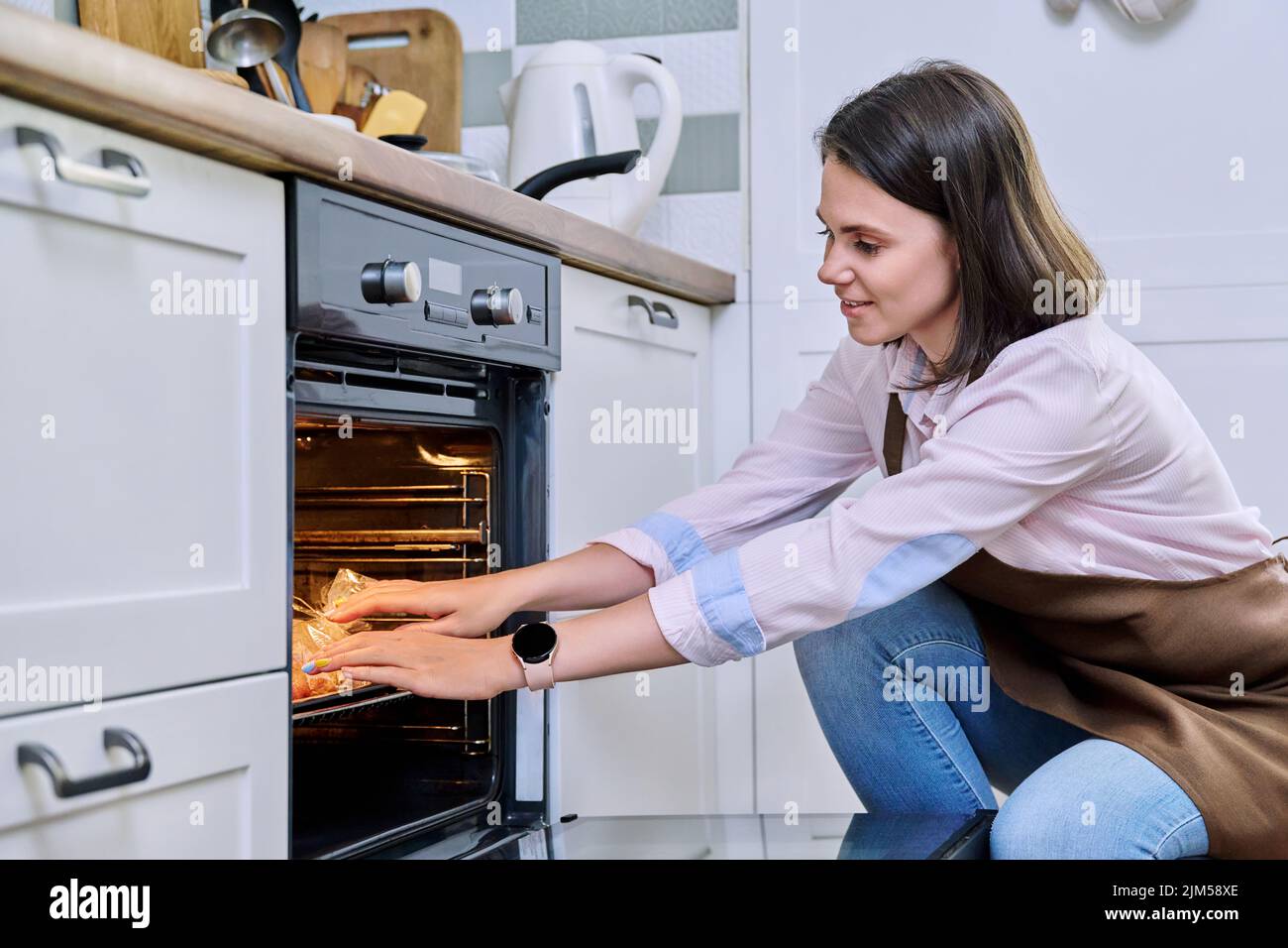 Young woman cooking food in the oven at home in the kitchen Stock Photo ...