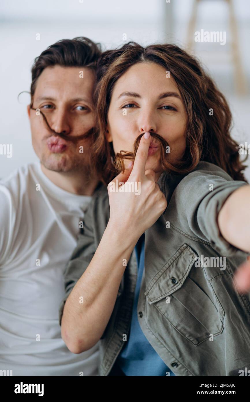 Happy newlyweds play and pose making mustaches with curly brunette hair ...