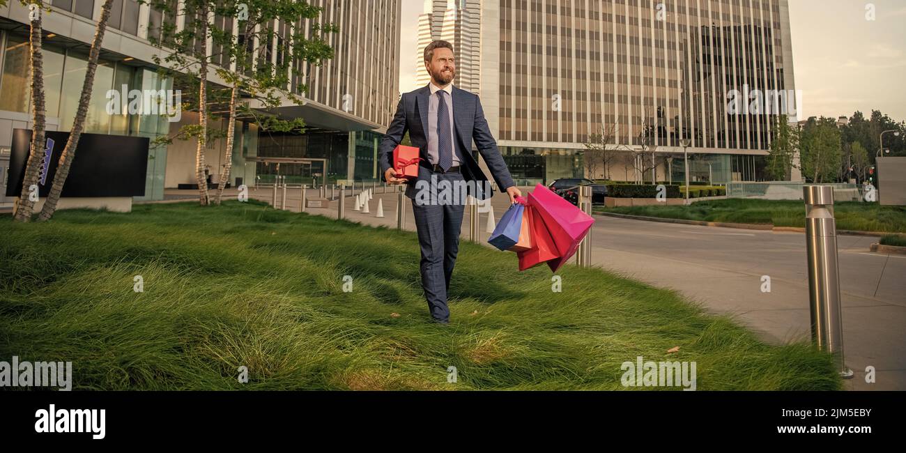 happy successful man in formalwear with shopping bags and present box ...