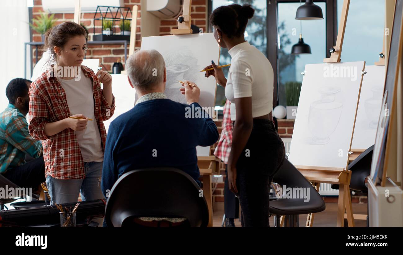 Diverse team of women giving drawing lesson to elder person attending ...