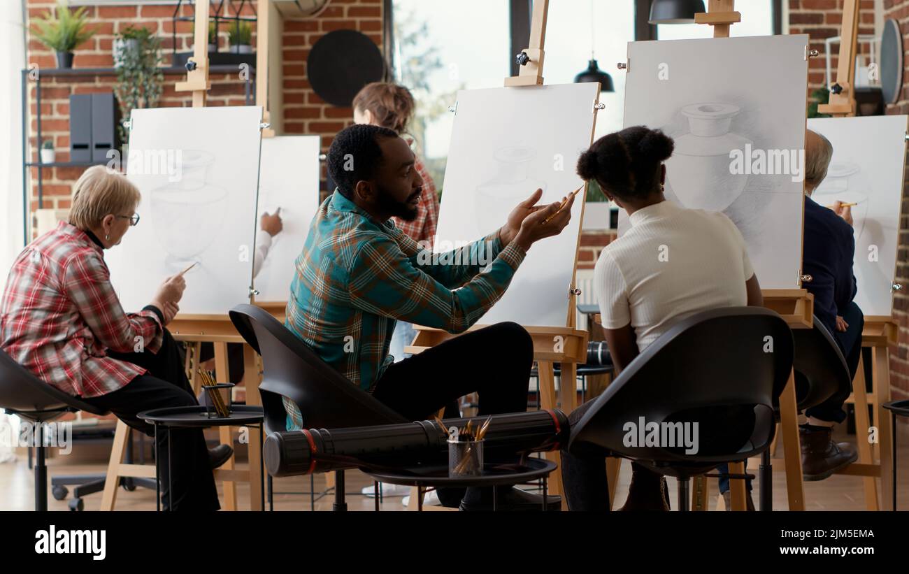 Young students drawing on canvas and talking about artwork in artistic ...