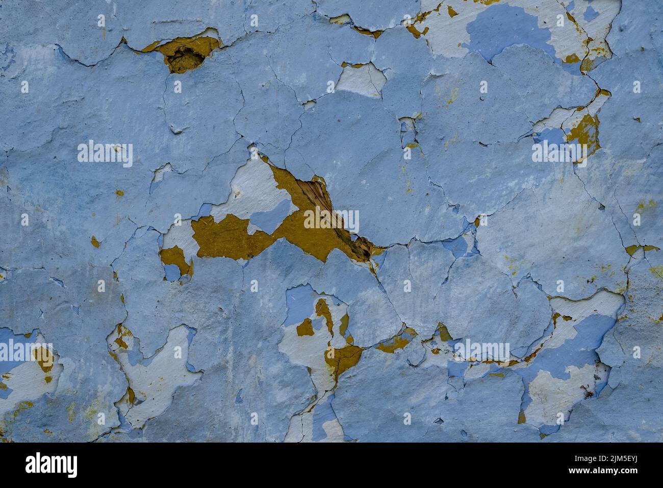 A close up shot of an old blue wall with cracks and paint chipping off ...