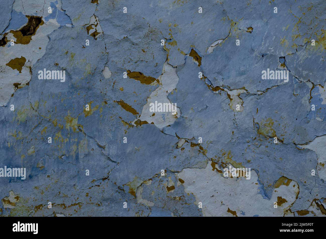 A close up shot of an old blue wall with cracks and paint chipping off ...