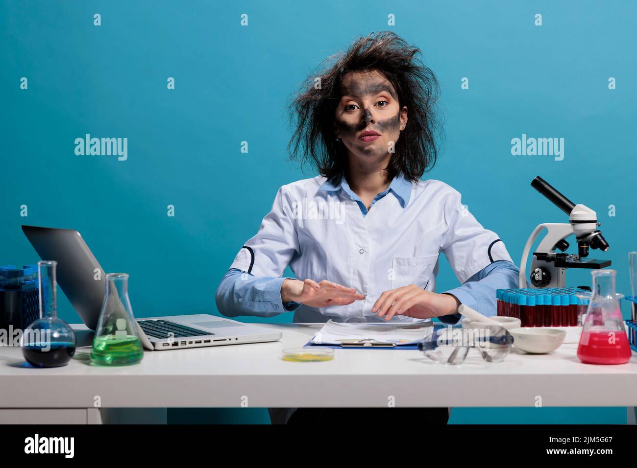 Mad silly looking scientist sitting at desk in laboratory with messy ...