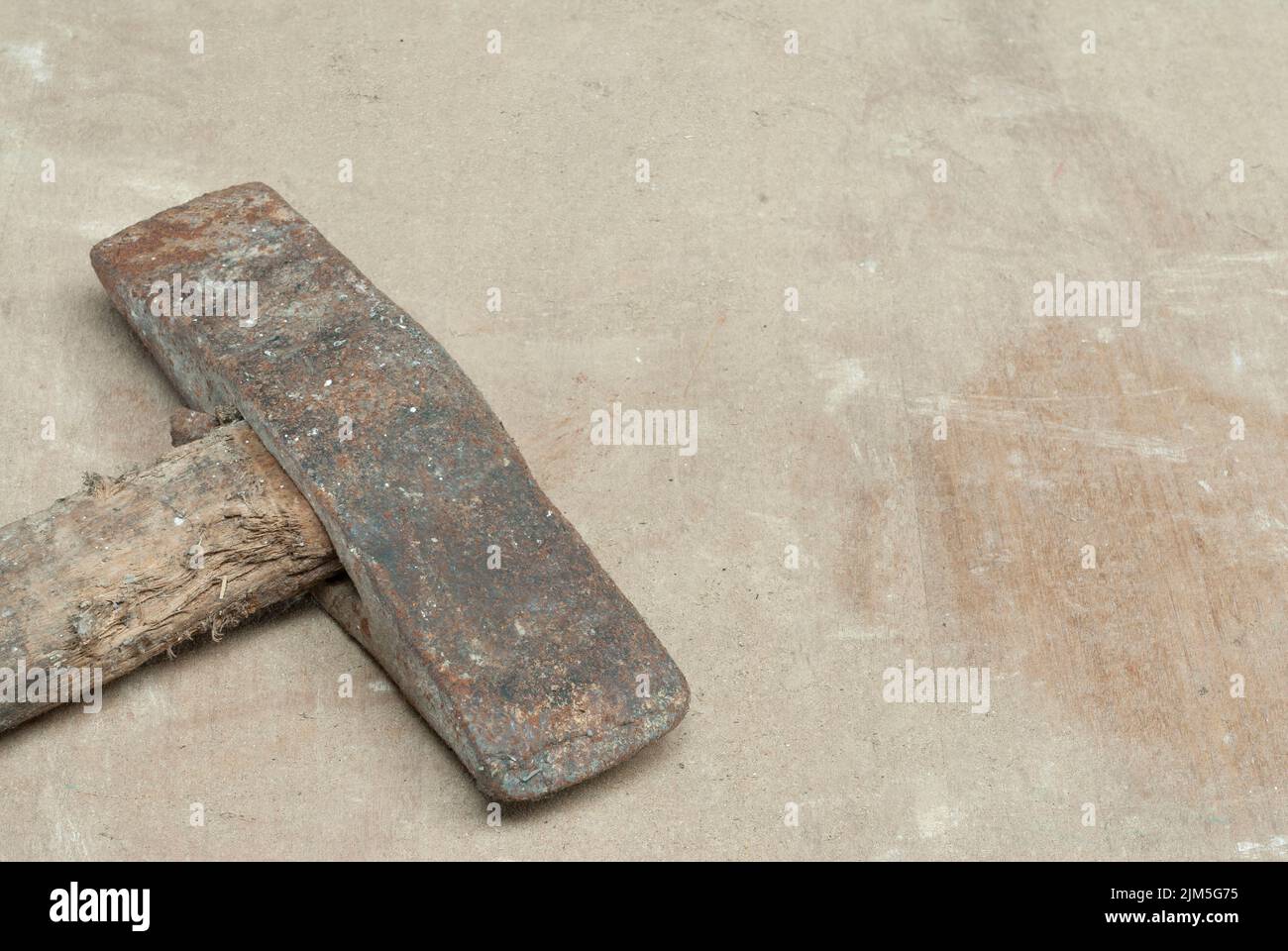 An old rusty steel hammer with a wooden handle on a light brown surface ...