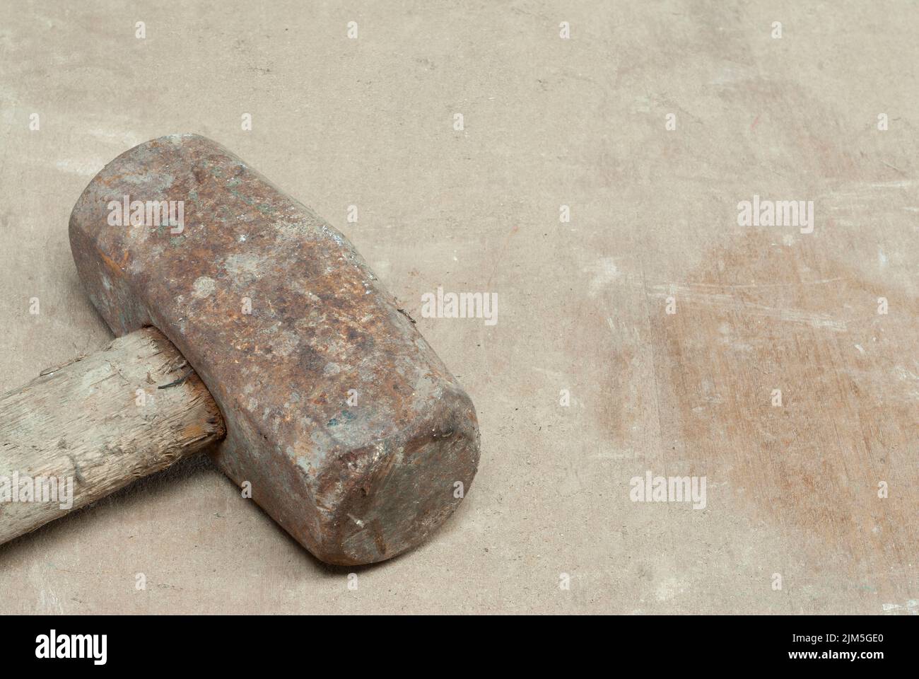 An old rusty steel hammer with a wooden handle on a light brown surface ...