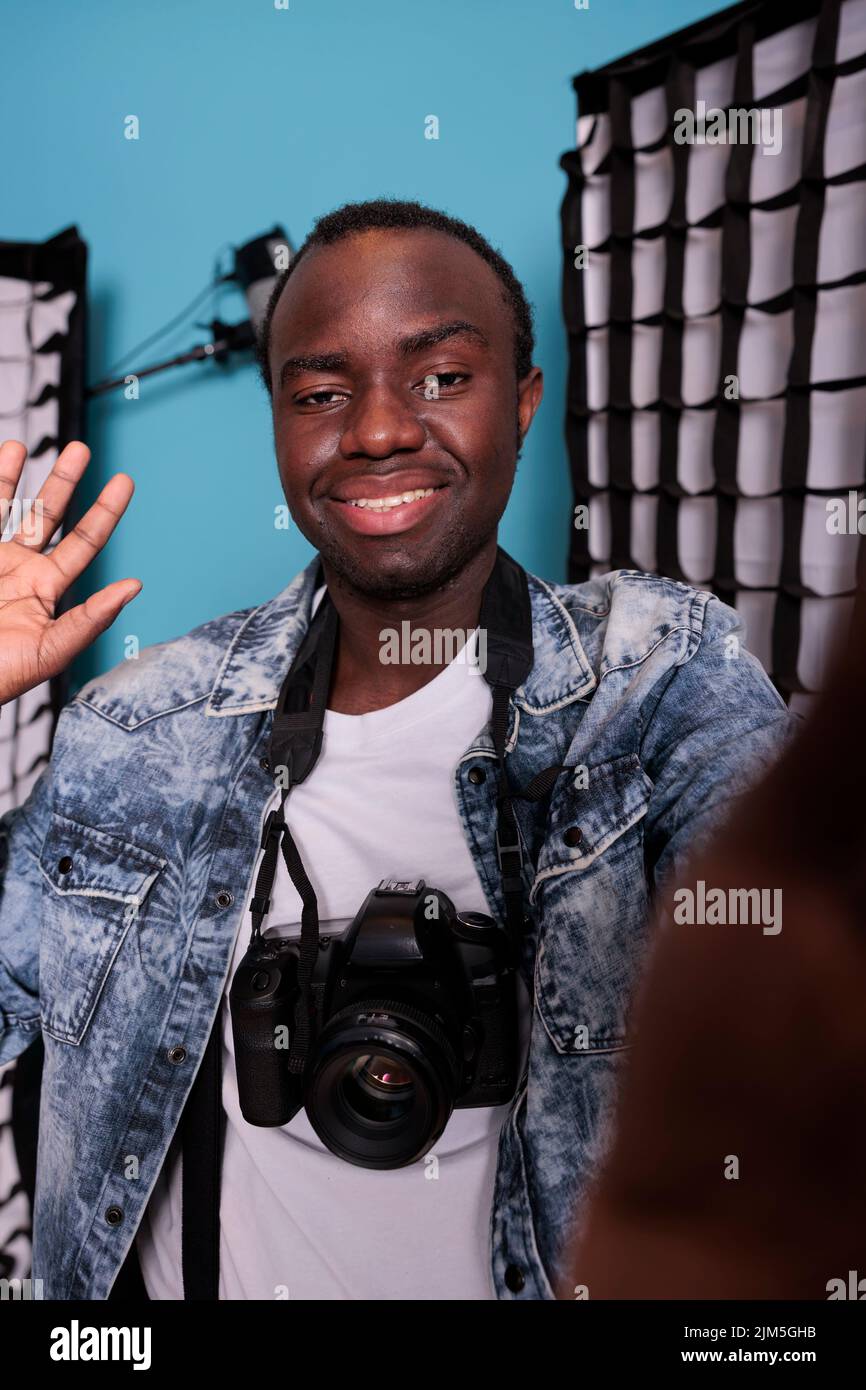 Happy african american photographer waving at camera while taking ...