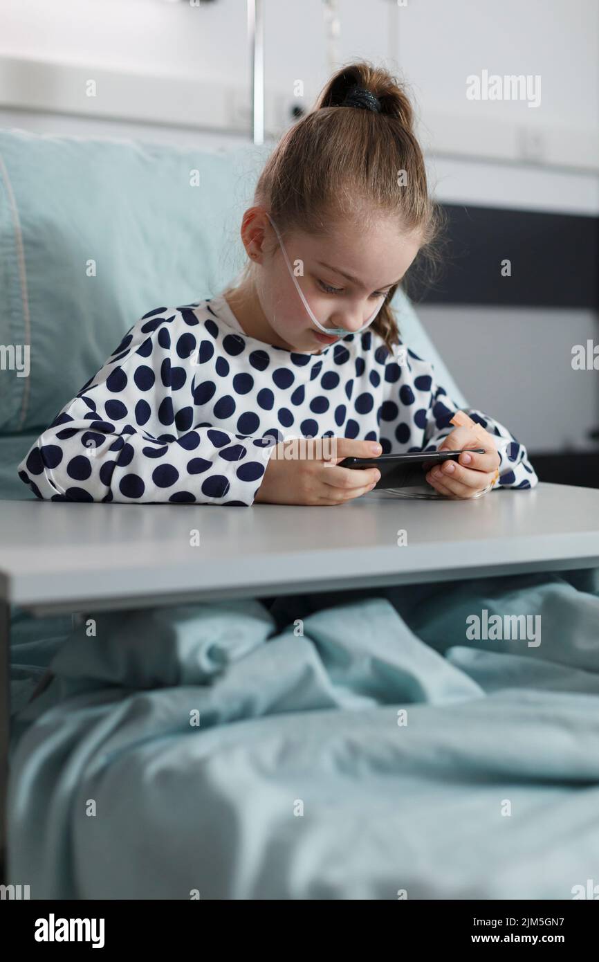 Hospitalized ill kid playing games on modern mobile phone while resting ...