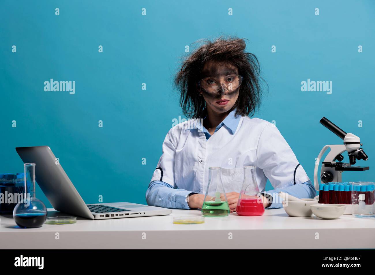 Foolish lab worker with wacky hair and dirty face sitting at desk on ...