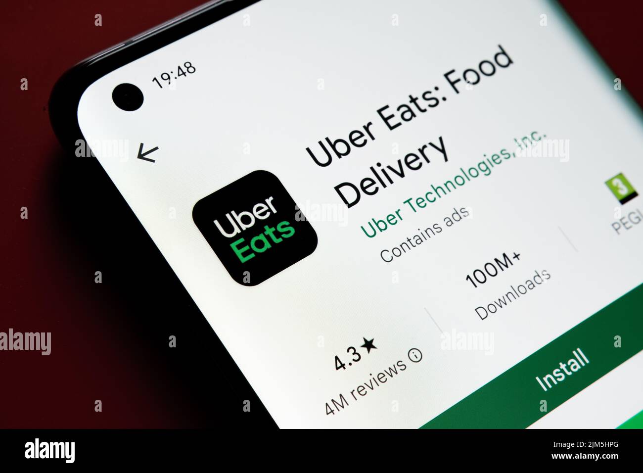 uber eats app seen in Google Play Store on the smartphone screen placed on red background. Close ...