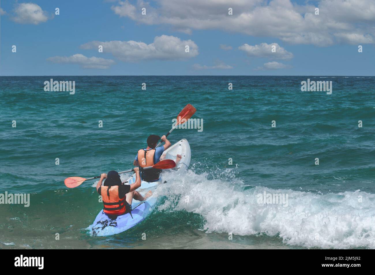 Two kayakers are trying to pass a large coastal wave and swim out into ...