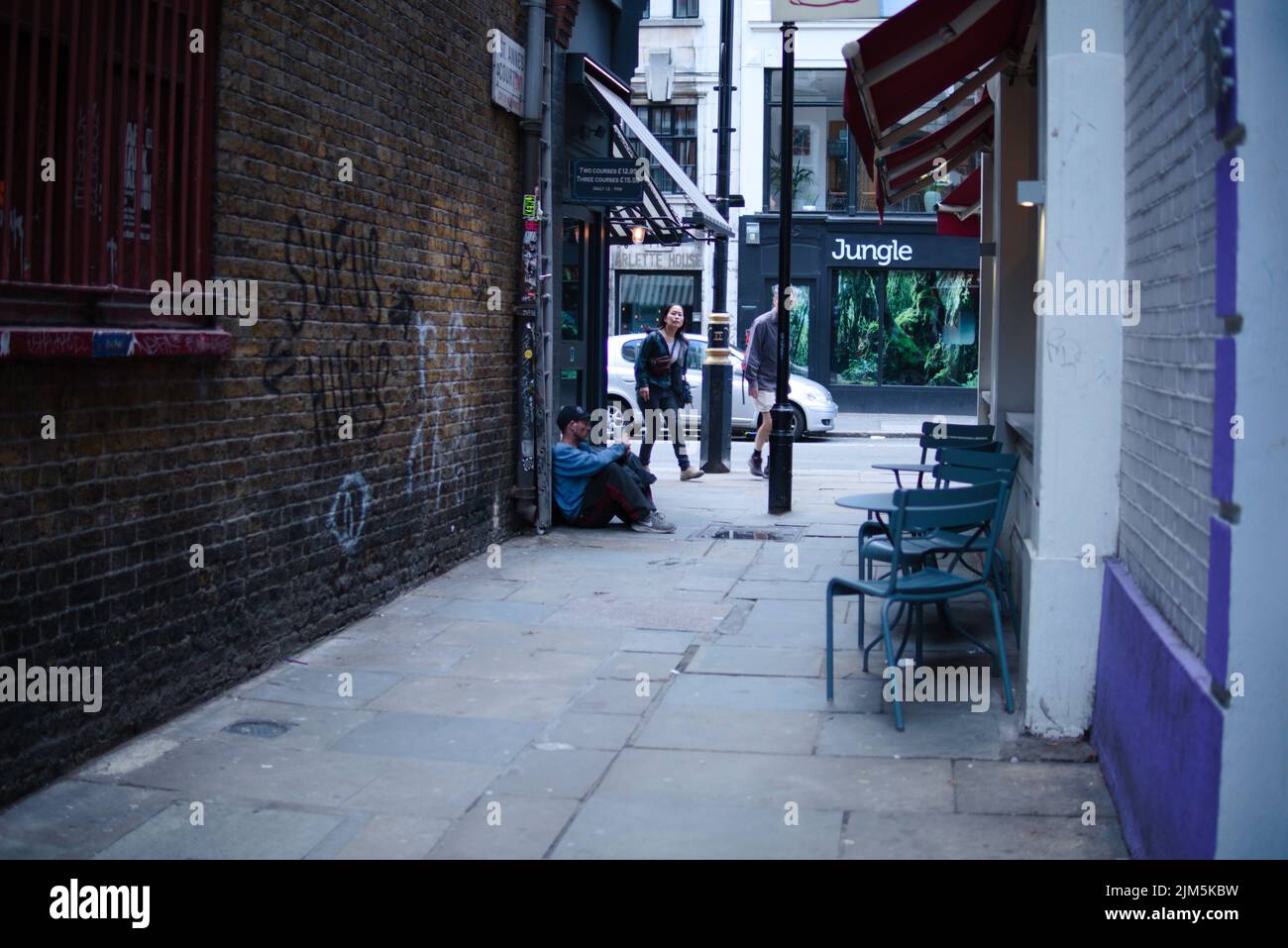 A small side street between buildings and a man sitting at the end of ...