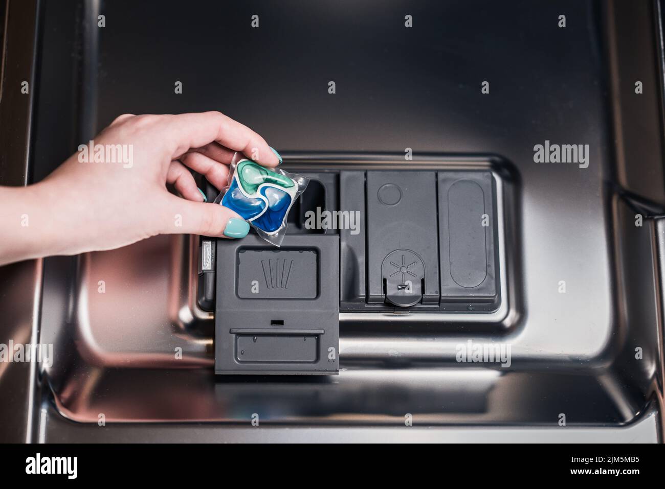 A female hand putting a colorful washing capsule into a dishwashing ...