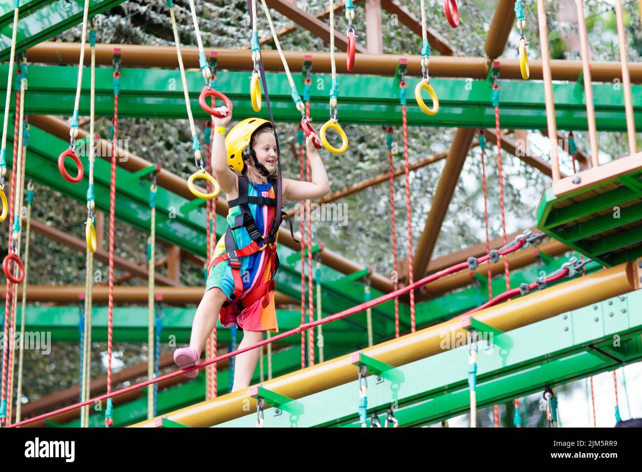 Child in forest adventure park. Kids climb on high rope trail. Agility ...