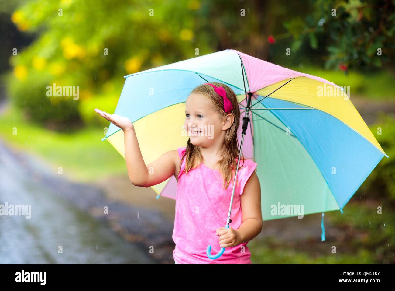 Kid playing out in the rain. Children with umbrella play outdoors in ...