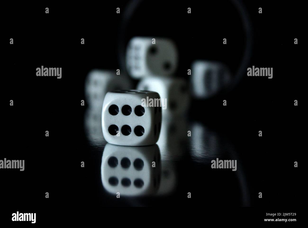 A white dice with six dots near a heap of dice on a black background ...