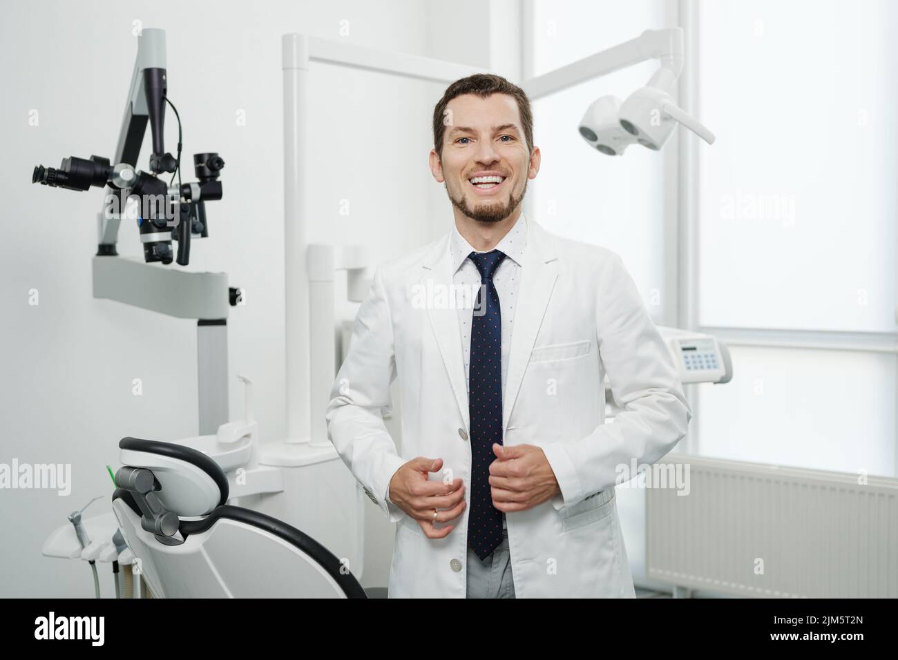 Portrait of happy male dentist wearing lab coat in white dental clinic ...
