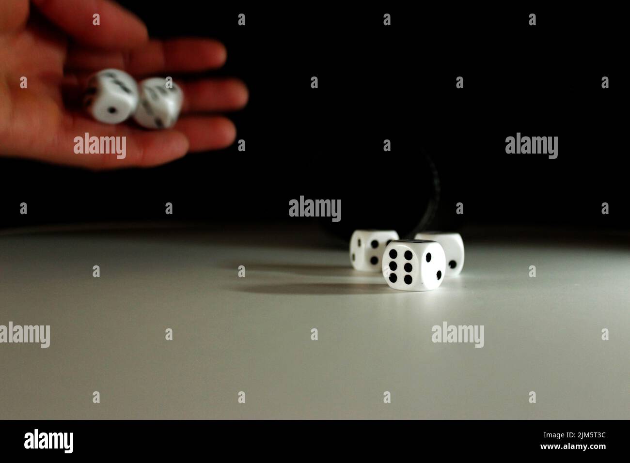 A hand rolling two dice near other dice on a white surface Stock Photo ...