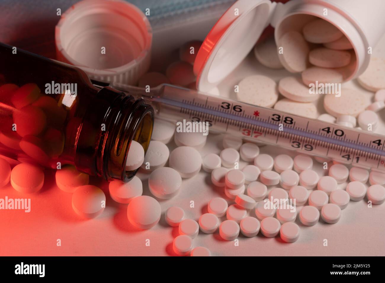White Pills with fever thermometer on top. Many pills and tablets on ...