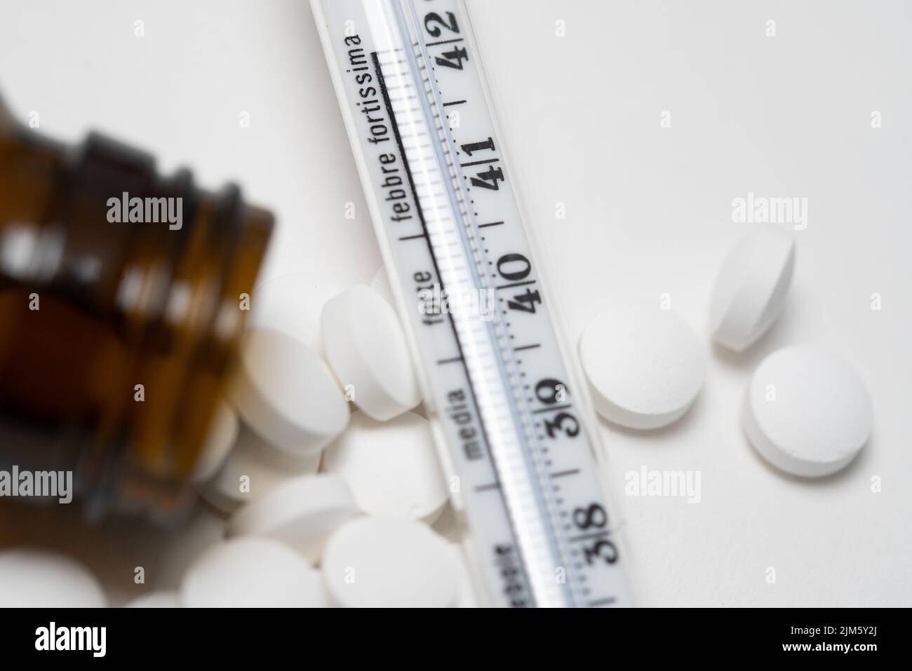Mercury in glass thermometer on white surface with medicine and pills ...
