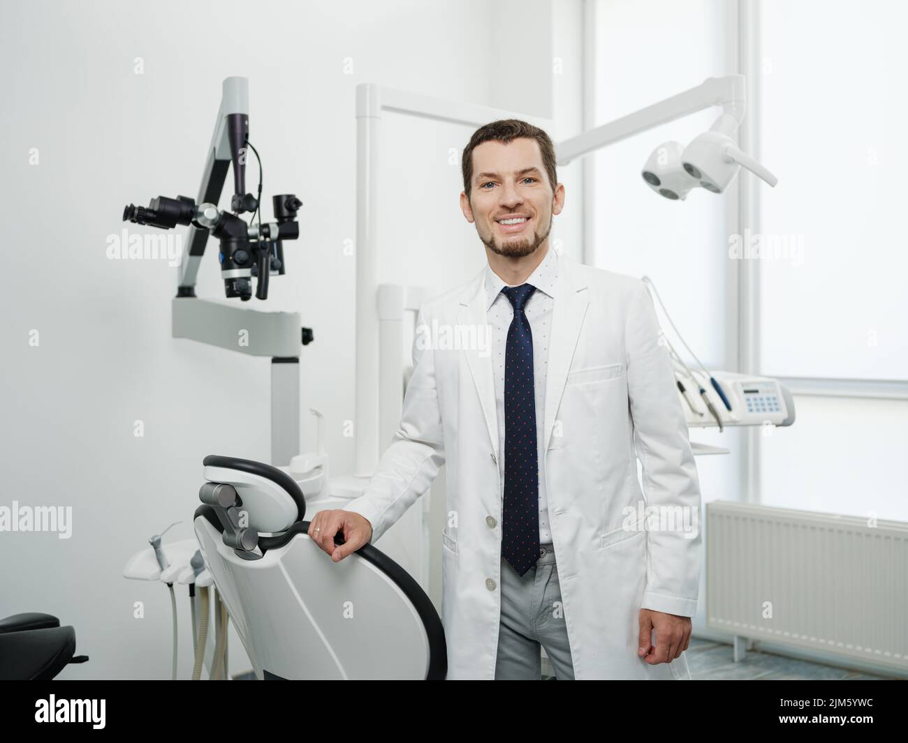 Portrait of happy male dentist wearing lab coat in white dental clinic ...