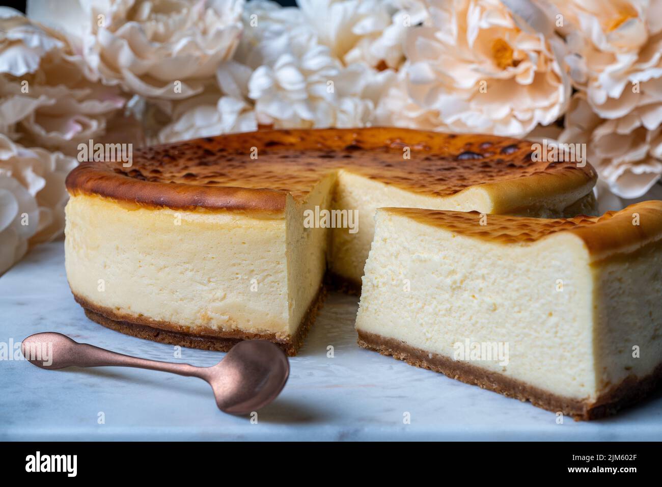 A round classic cheesecake sliced on a marble cake stand and flowers on ...