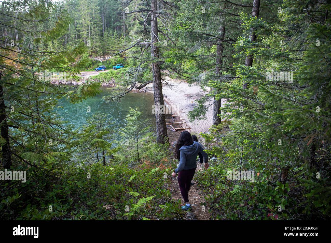 Two people walking towards a lake surrounded by trees in a forest with ...