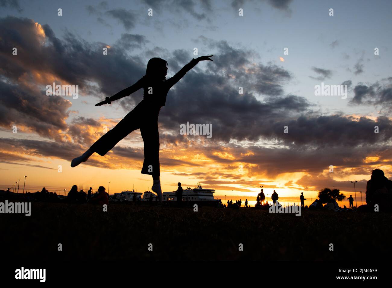 A silhouette of a girl dancing and jumping in the air on a sunset sky ...