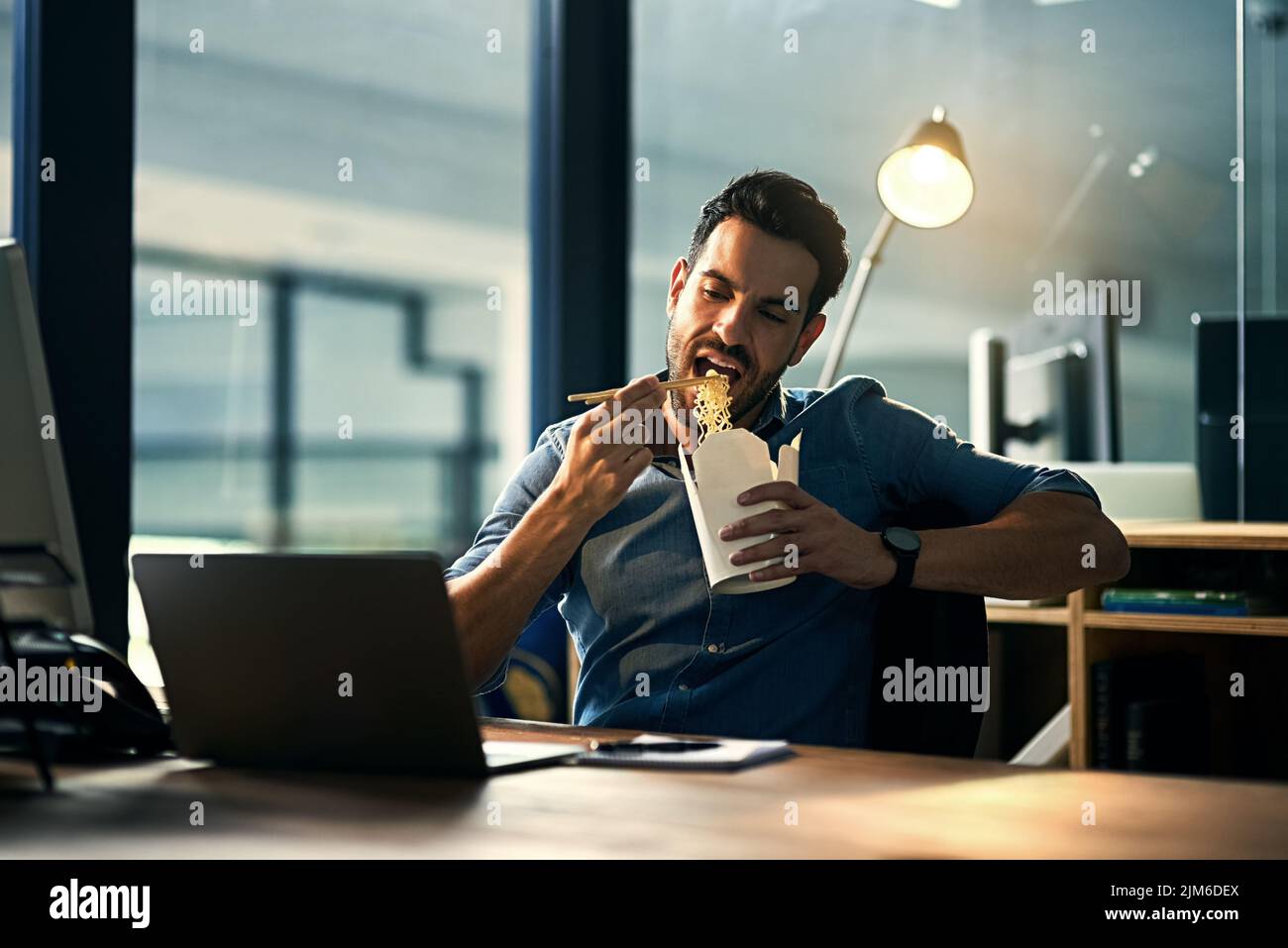 Young hungry businessman working late and eating at desk. Man having ...