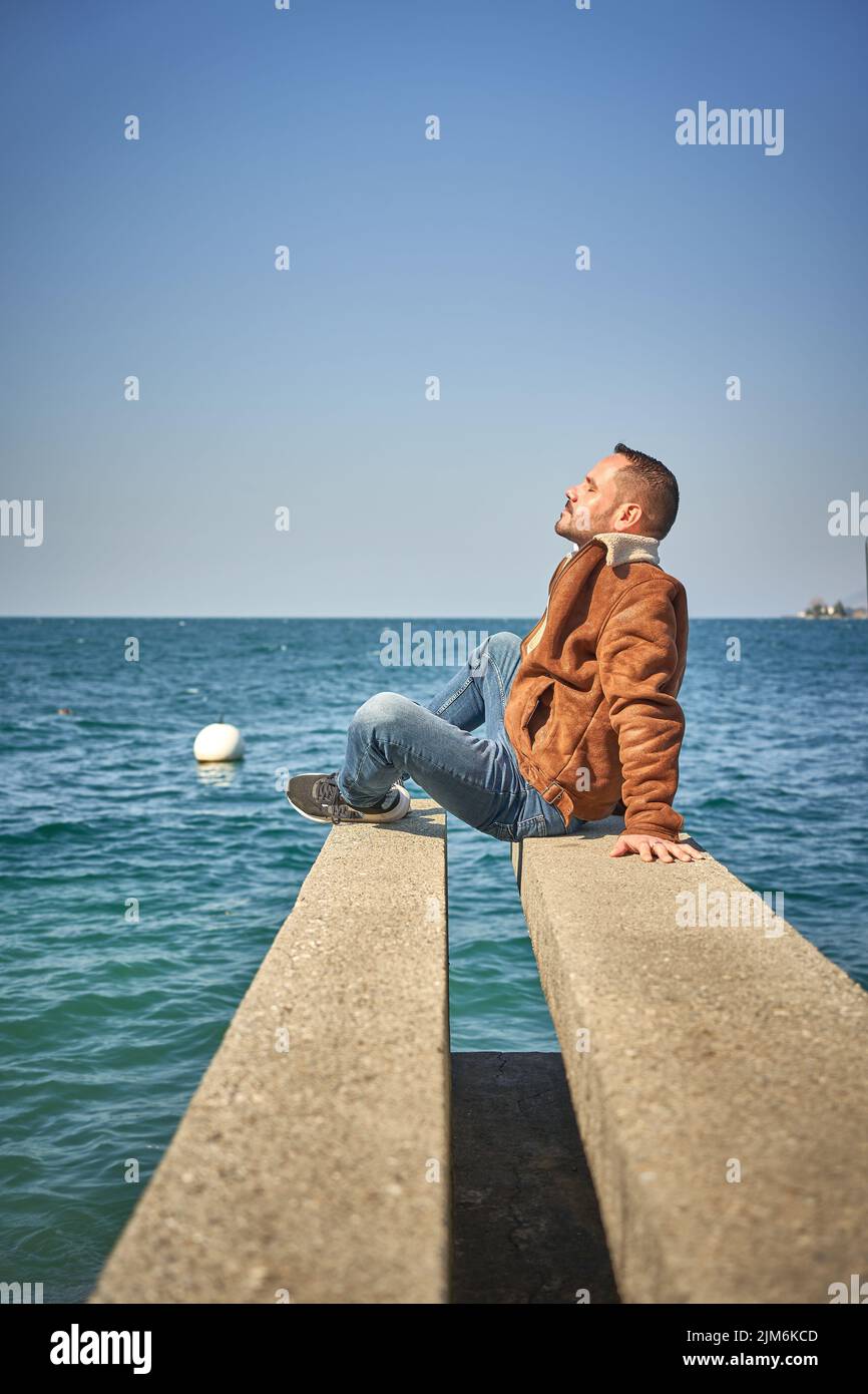 A vertical shot of a young Caucasian male sitting at the edge of a ...