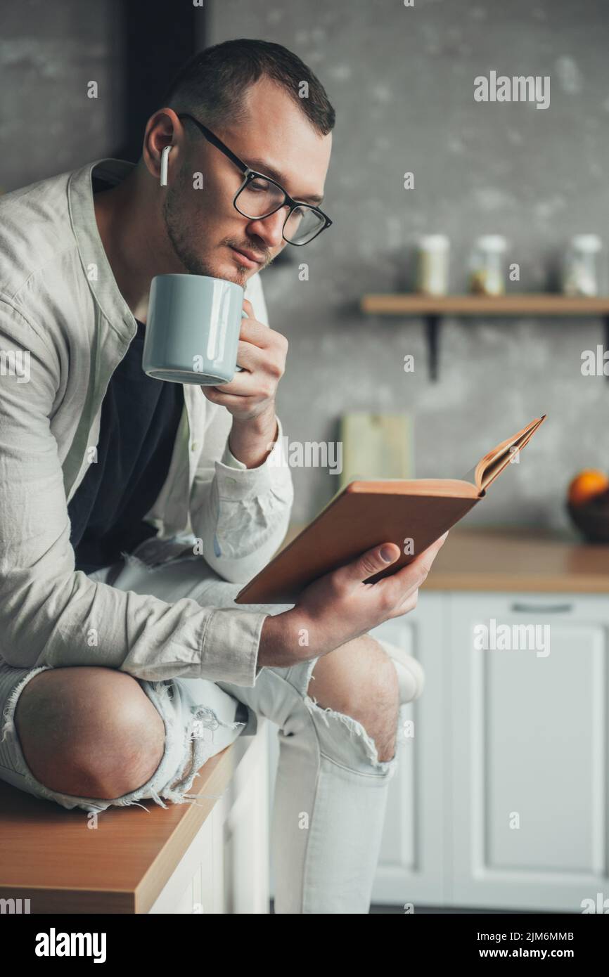 Man drinking morning tea in the kitchen reading paper book. Cozy home ...