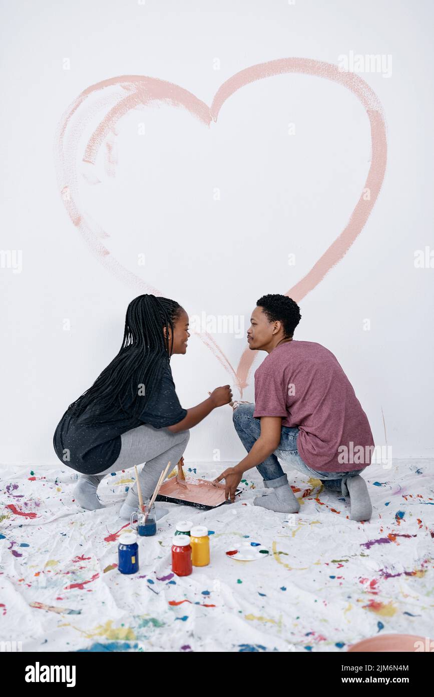 Art is love and love is art. a young couple painting a heart on a wall ...