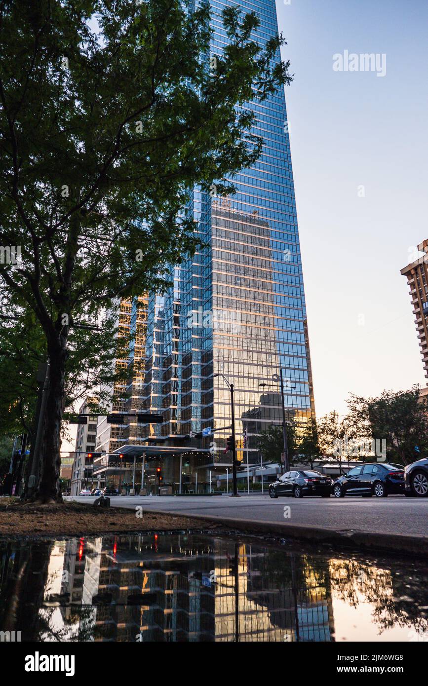 A high rise building and cars on the street with reflection on puddle ...