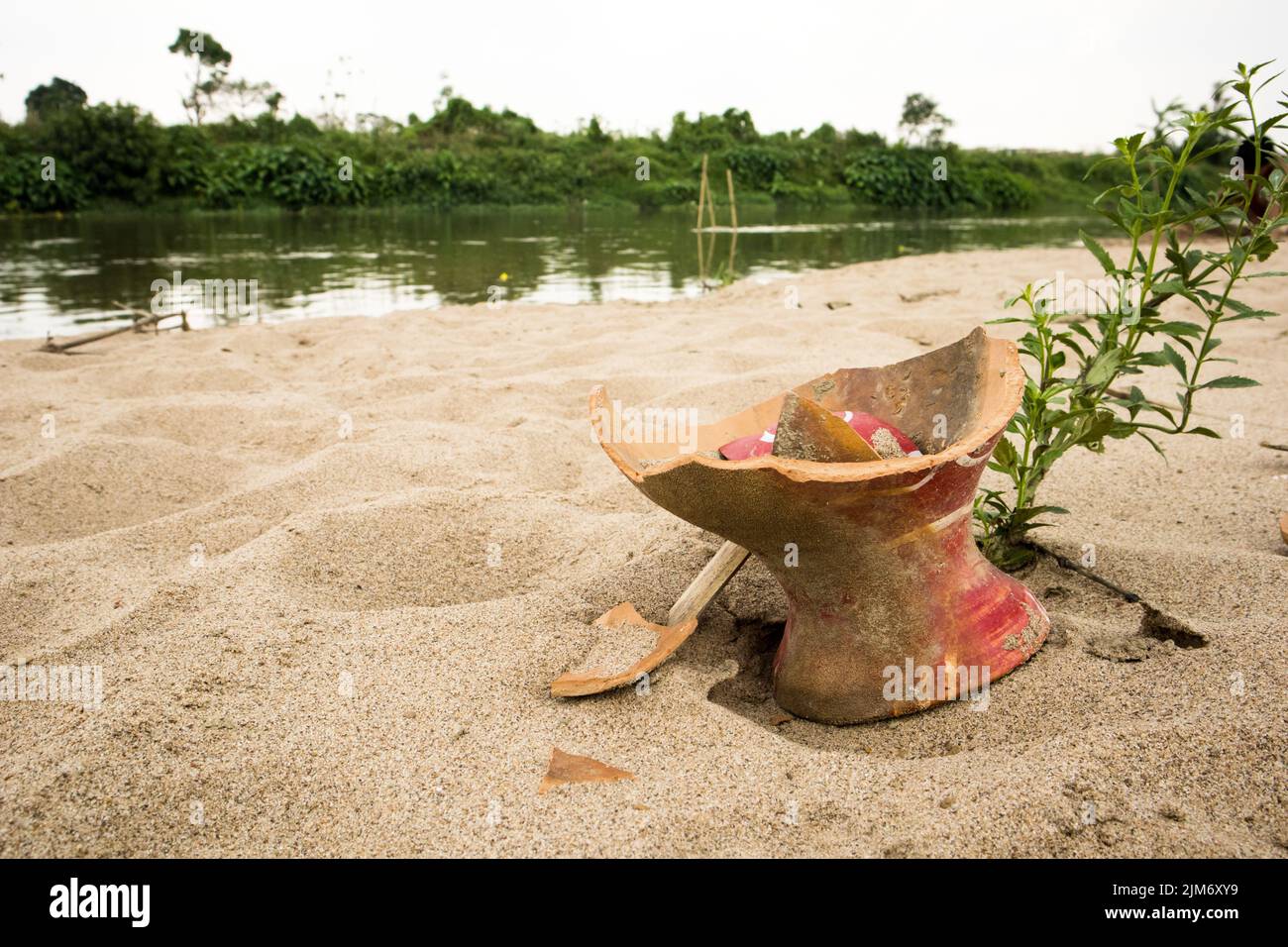 A lonely plant and a broken pot in the sand of a river-bank in the ...