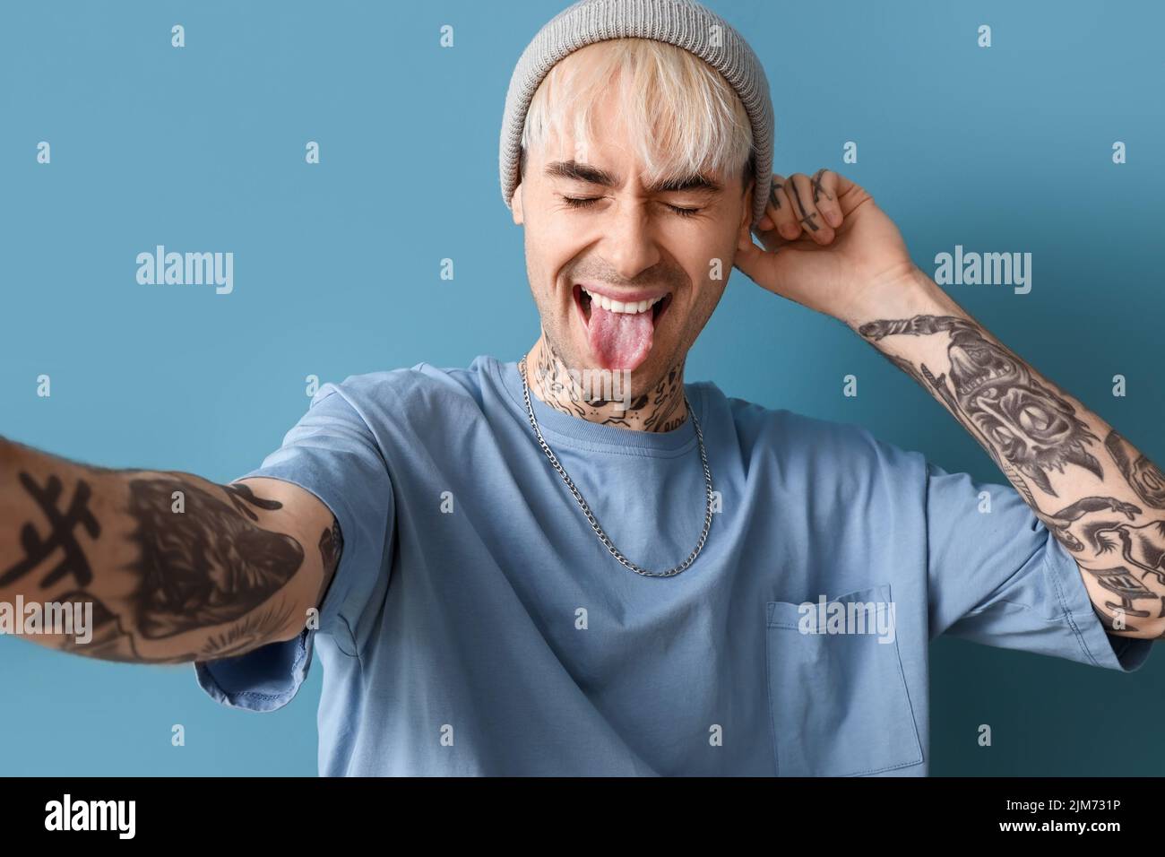 Young tattooed man showing tongue on blue background Stock Photo - Alamy