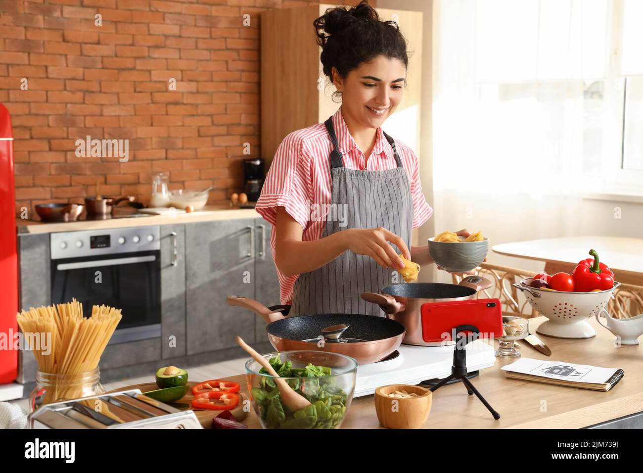 Young woman cooking pasta while watching video tutorial in kitchen ...