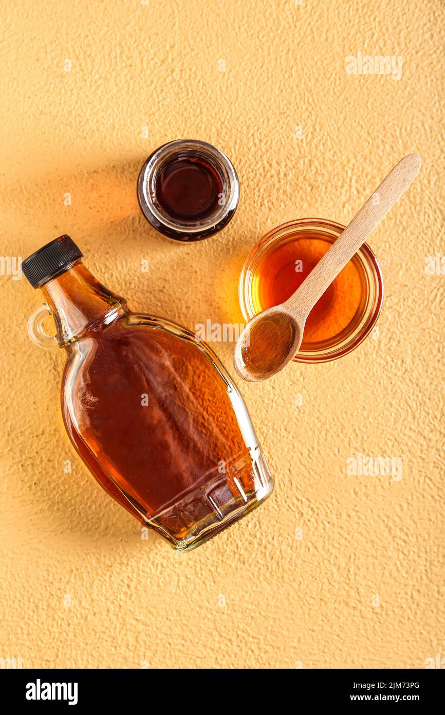 Bottles and bowl of maple syrup on color background Stock Photo - Alamy